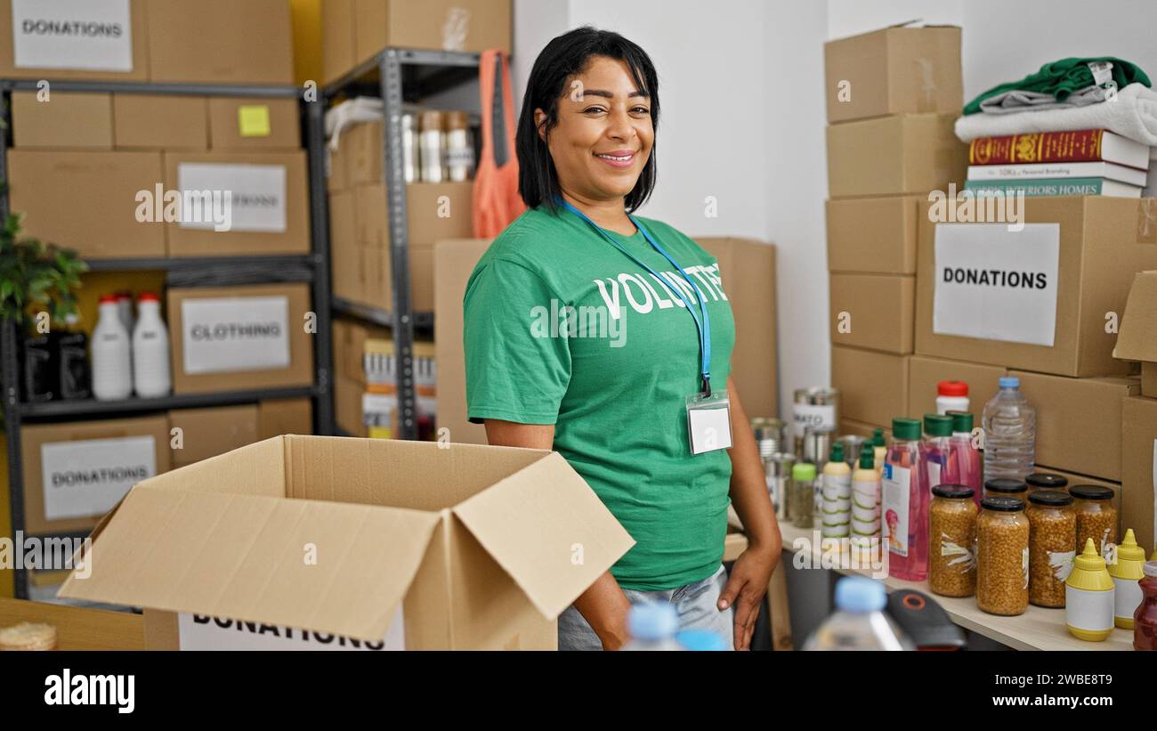 A smiling middle-aged hispanic woman volunteers sorting donations in a ...
