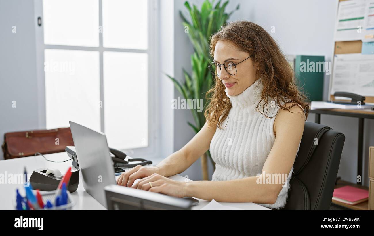 Focused hispanic woman working on a laptop in a modern office setup ...