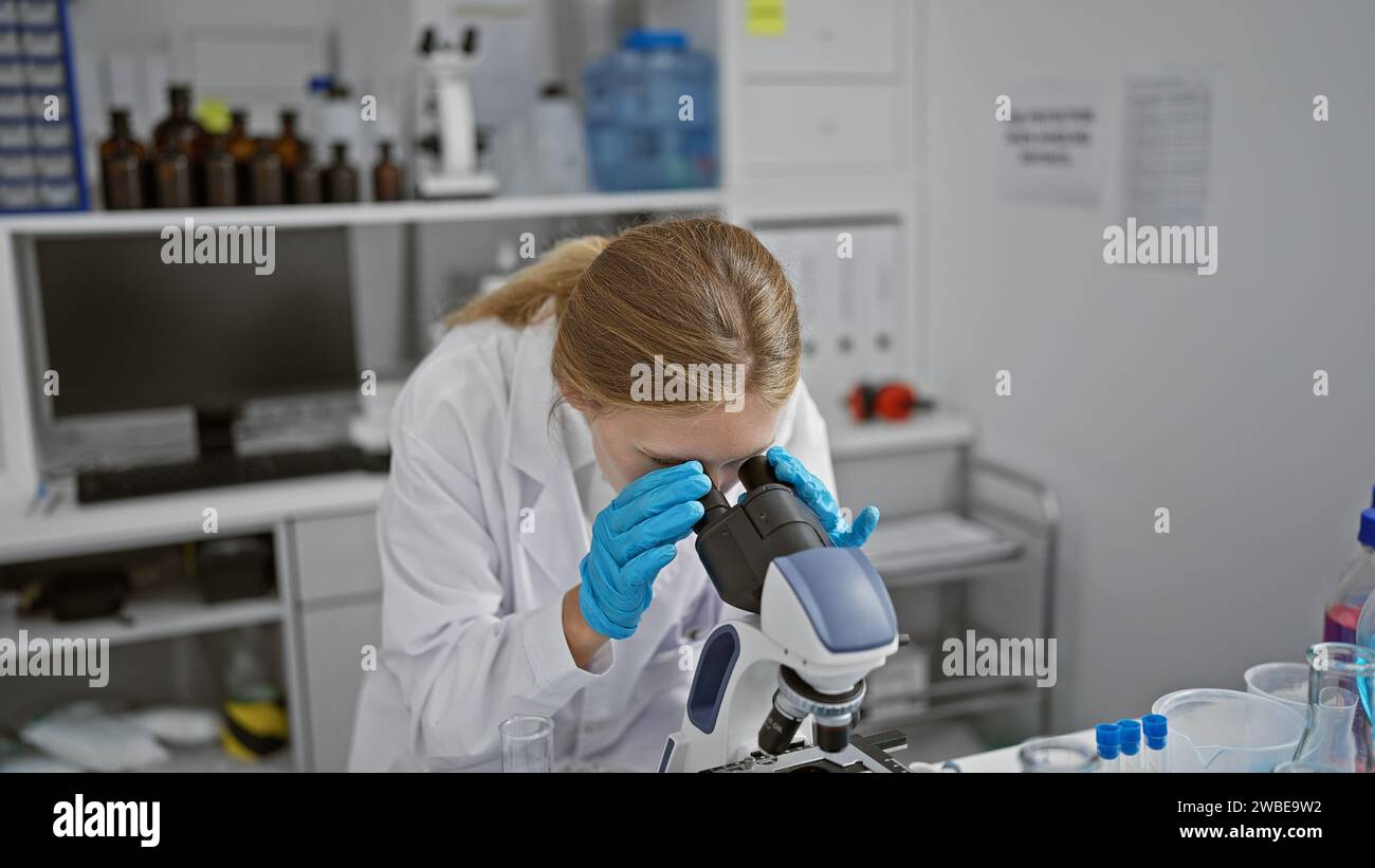 A focused young woman scientist examines samples through a microscope ...