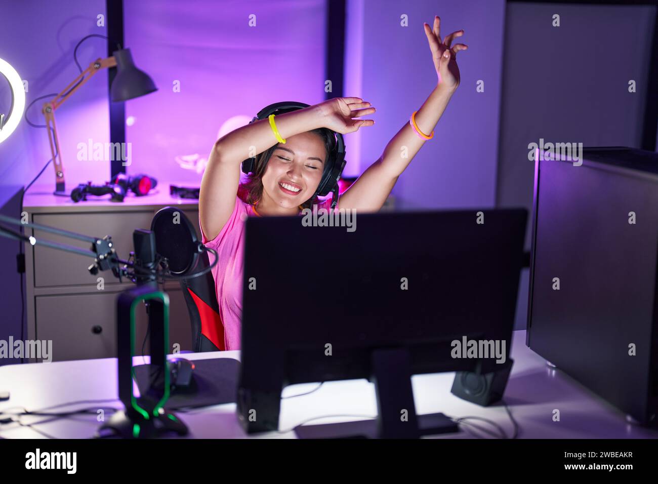 Young hispanic woman streamer playing video game dancing at gaming room ...