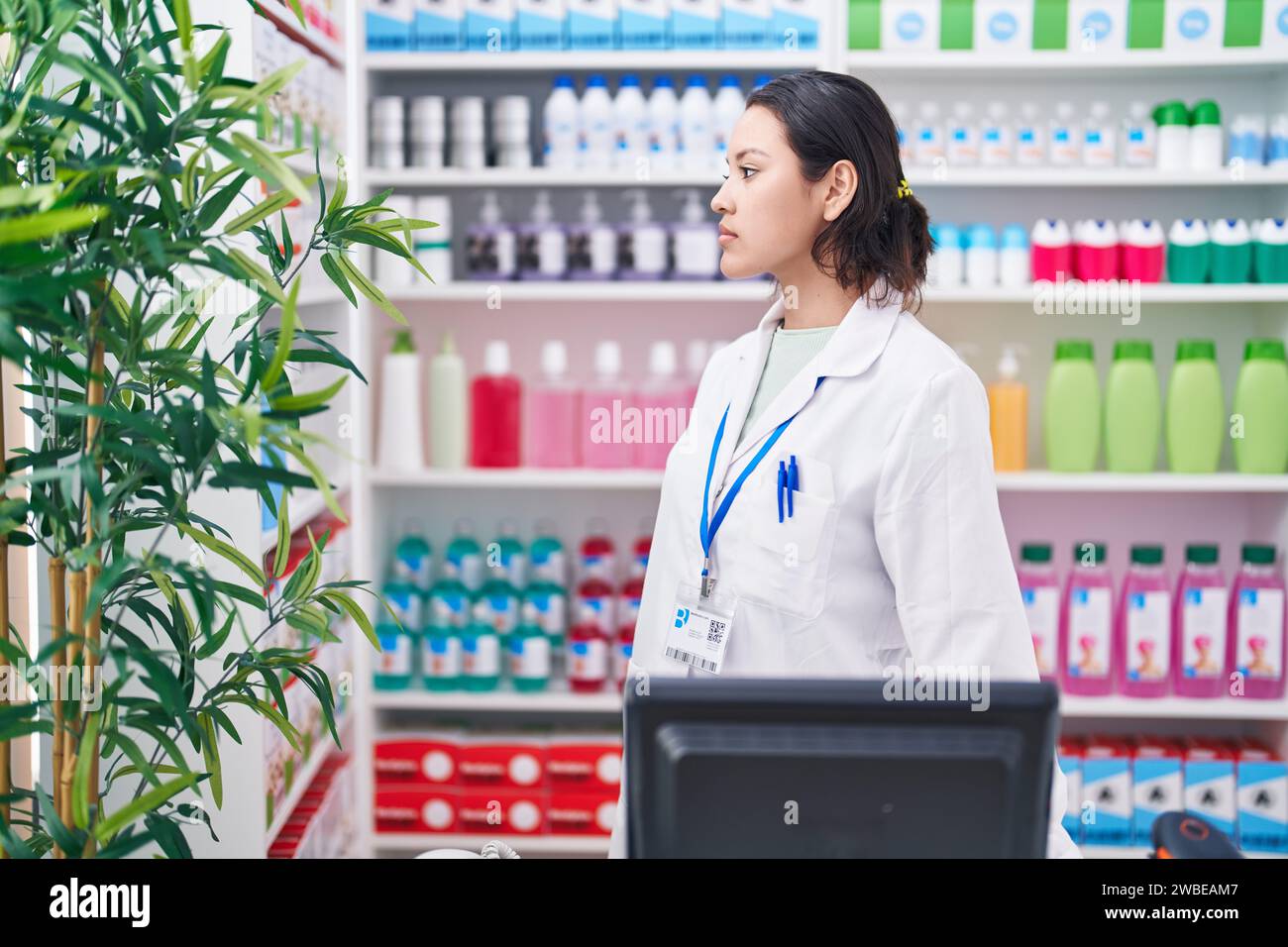Hispanic young woman working at pharmacy drugstore looking to side ...