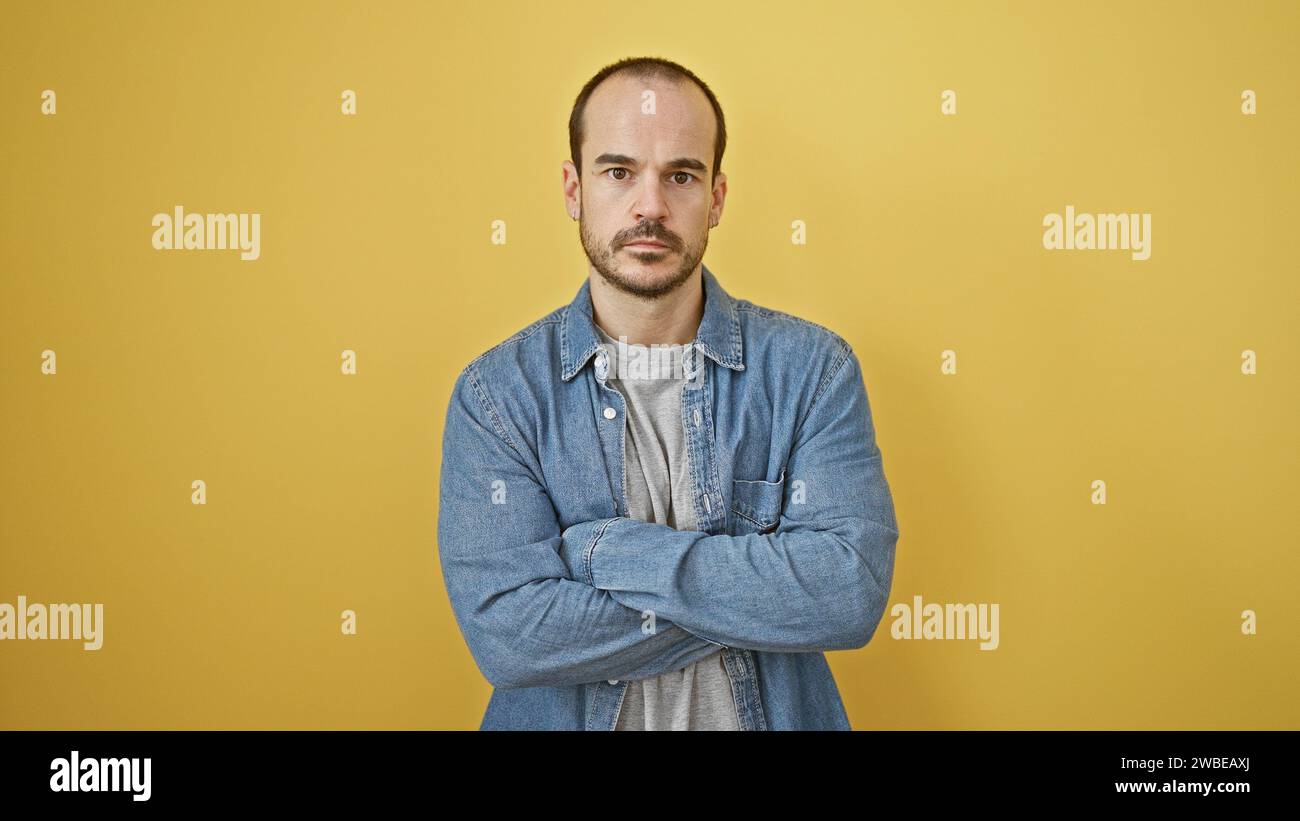 A bald hispanic man with a beard, wearing a denim shirt, stands with ...
