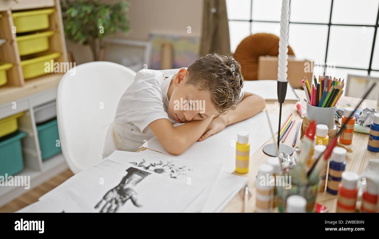 Adorable blond boy artist, leaning on table, sleeping after a tiring ...