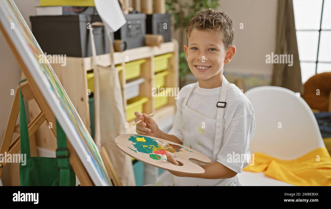 Adorable blond boy artist, confidently smiling as he enjoys drawing at ...