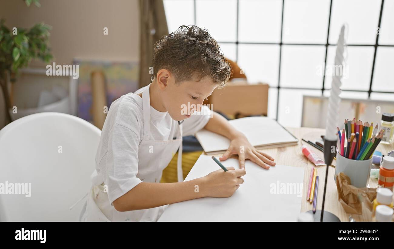 Adorable little blond boy artist intently drawing in his notebook ...