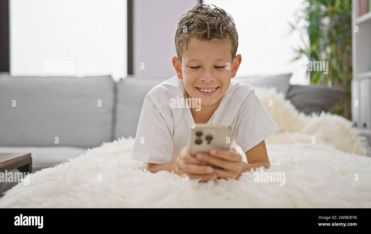 Adorable blond boy, full of joy, cheerfully using his smartphone ...