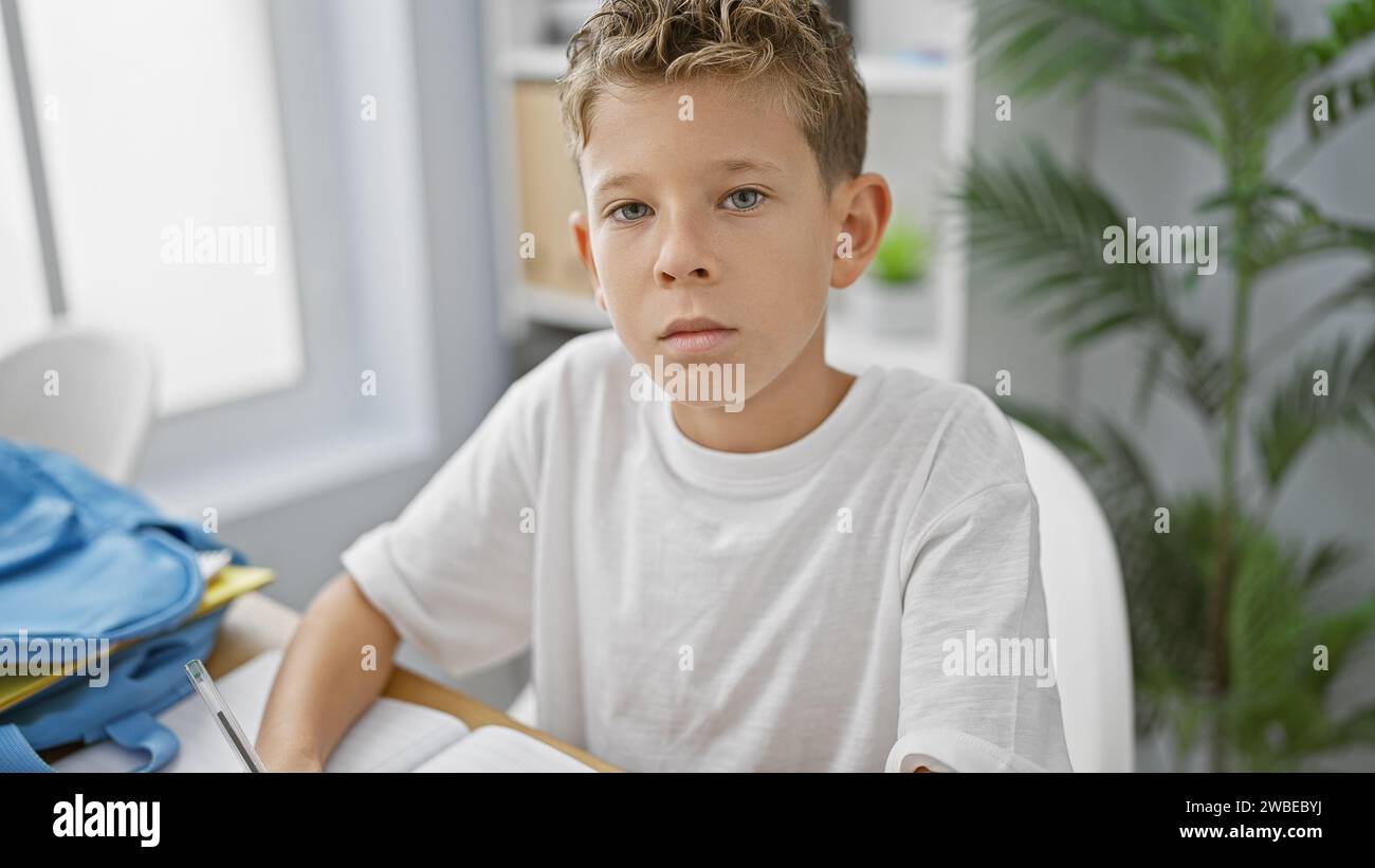 Adorable blond boy student concentrating and taking notes at his desk ...