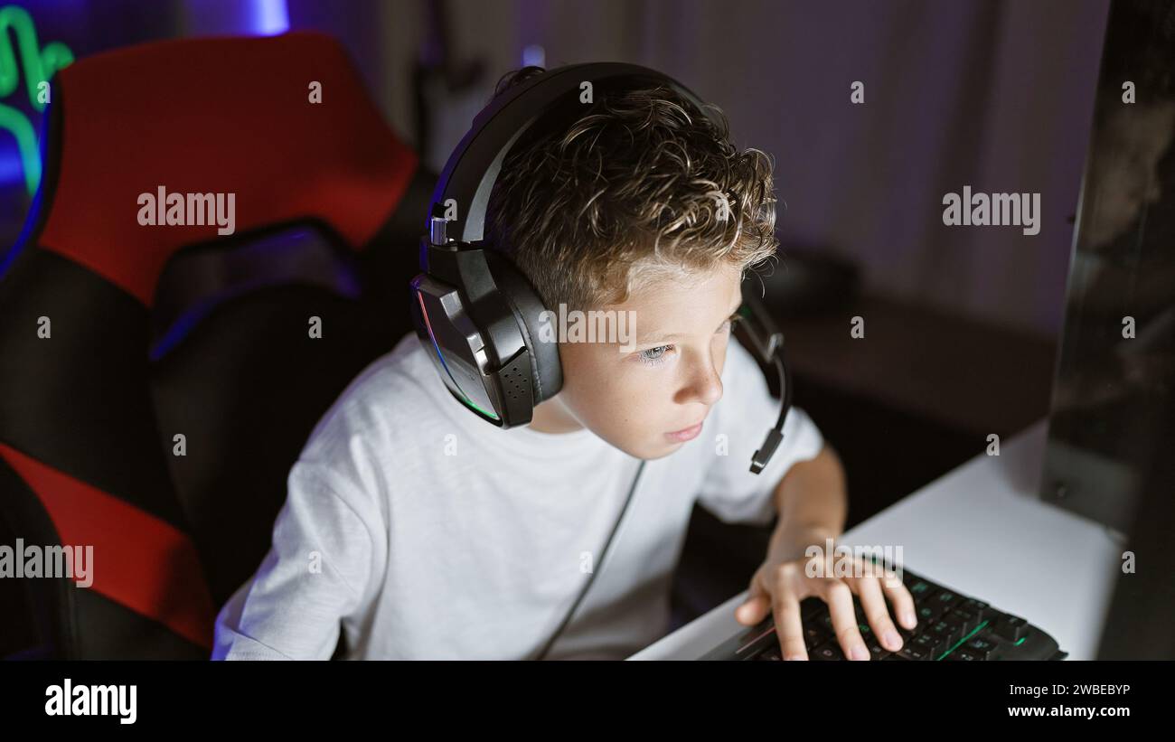 Adorable blond boy streamer, engrossed playing a futuristic video game ...