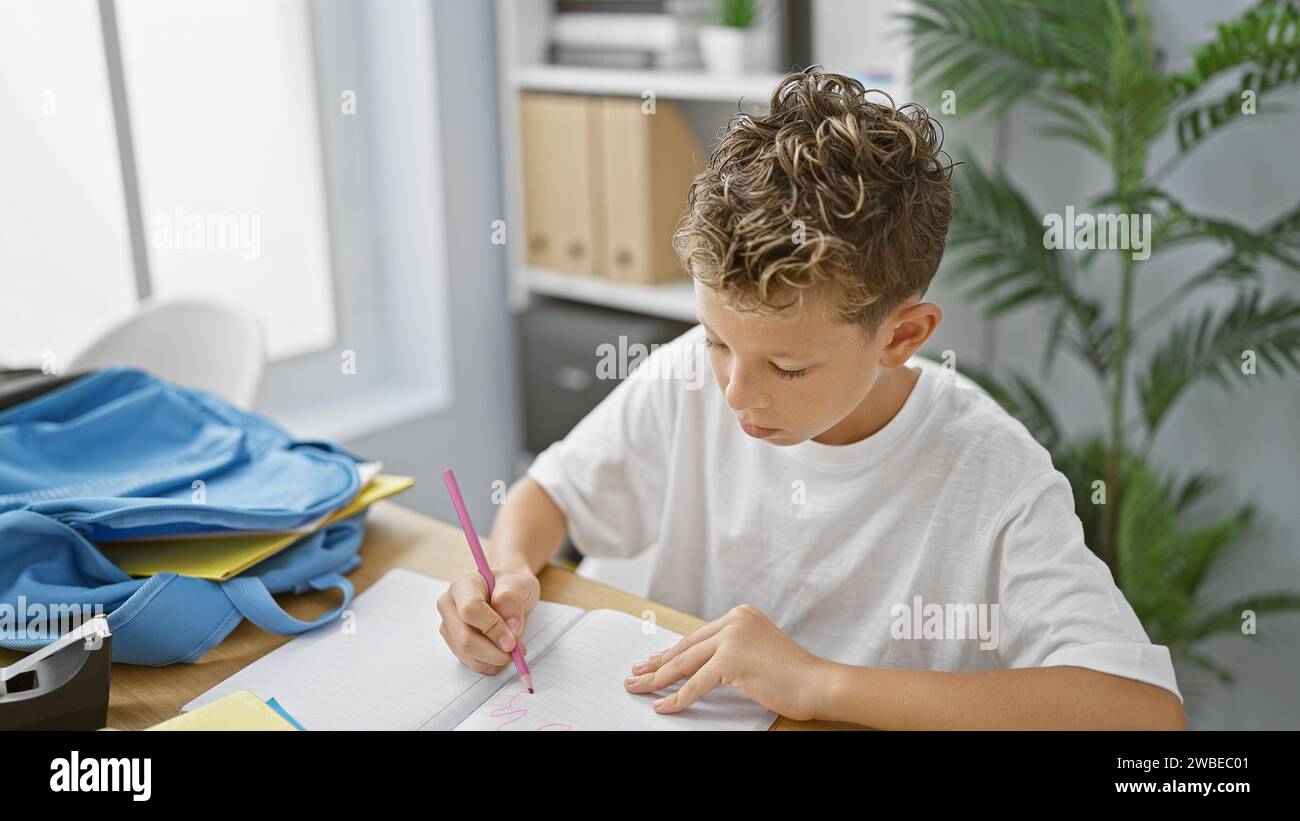 Adorable blond boy student concentrating and taking notes at his desk ...