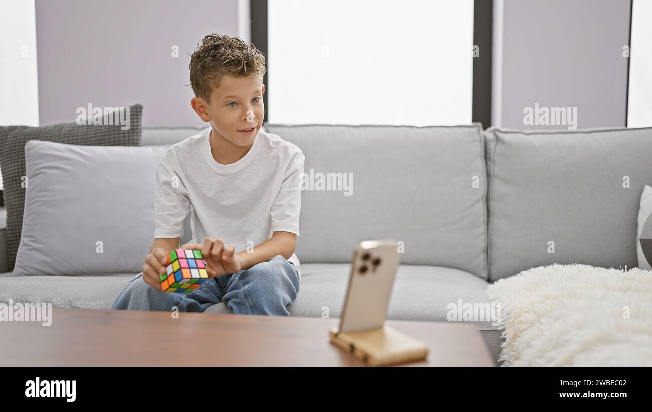 Adorable blond boy sitting on sofa, confidently solving rubik cube ...