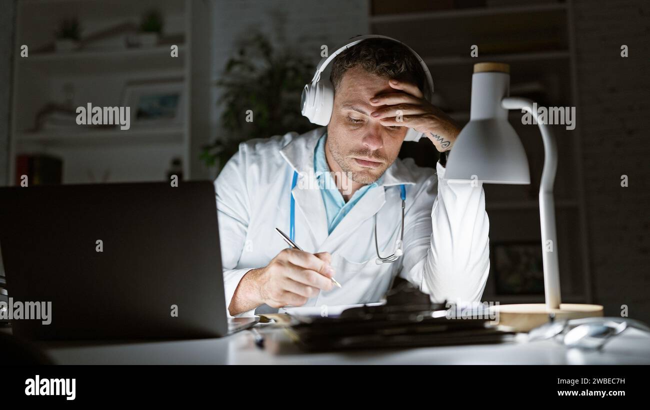 Stressed hispanic male doctor working late in a clinic office, wearing ...