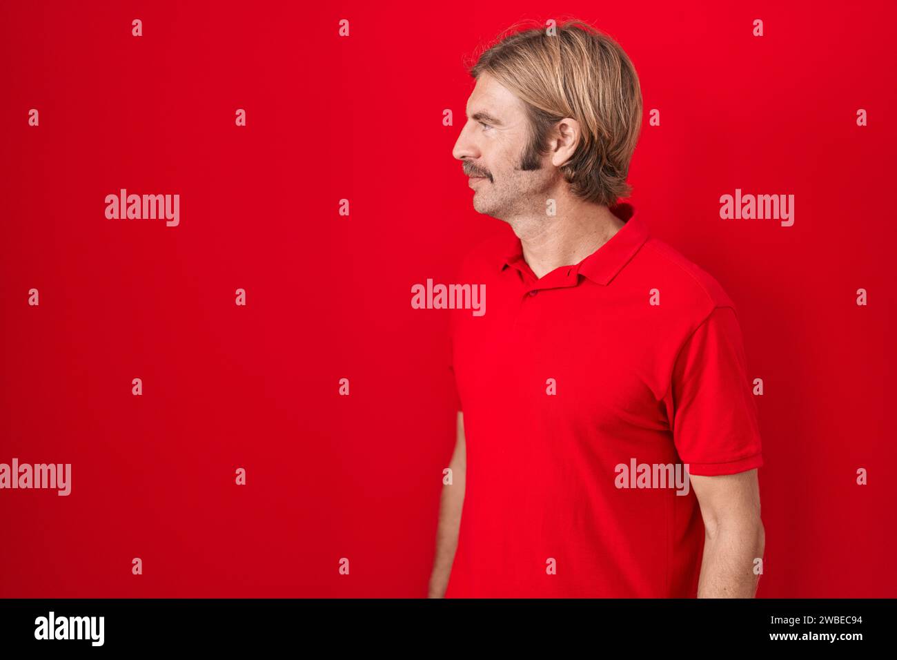Caucasian man with mustache standing over red background looking to ...