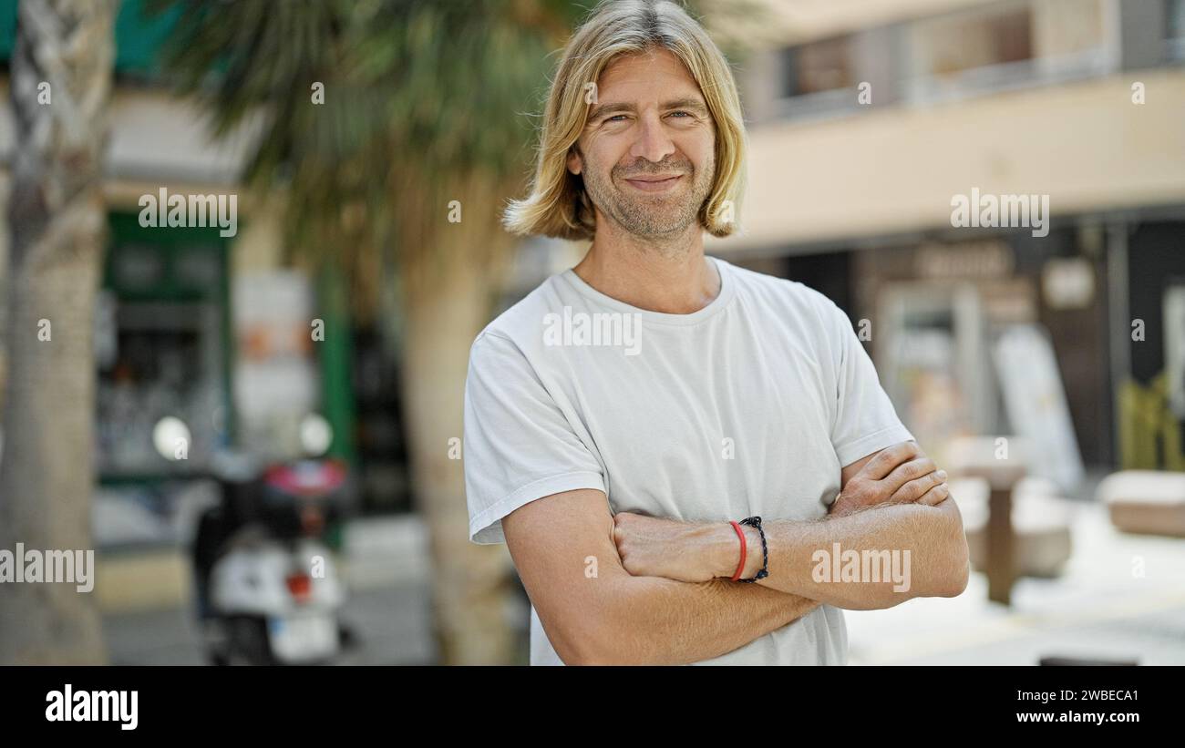 Blond man with long hair smiling confidently on an urban street ...