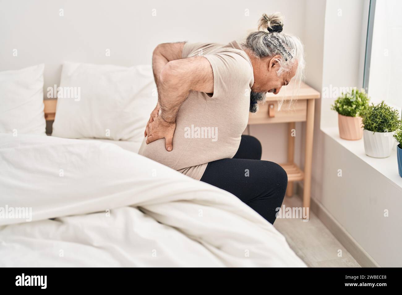 Middle age grey-haired man suffering for back injury sitting on bed at ...