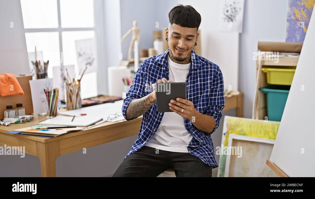 Handsome young latin artist confidently using touchpad, smiling while ...