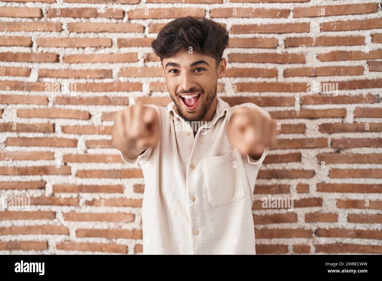 Arab man with beard standing over bricks wall background pointing to ...