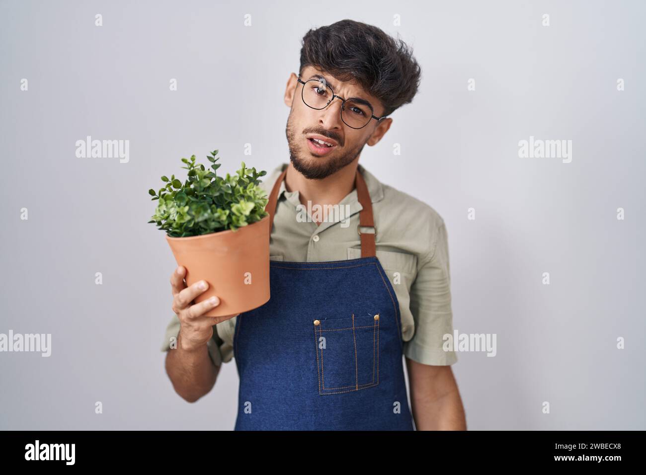 Arab man with beard holding green plant pot in shock face, looking ...