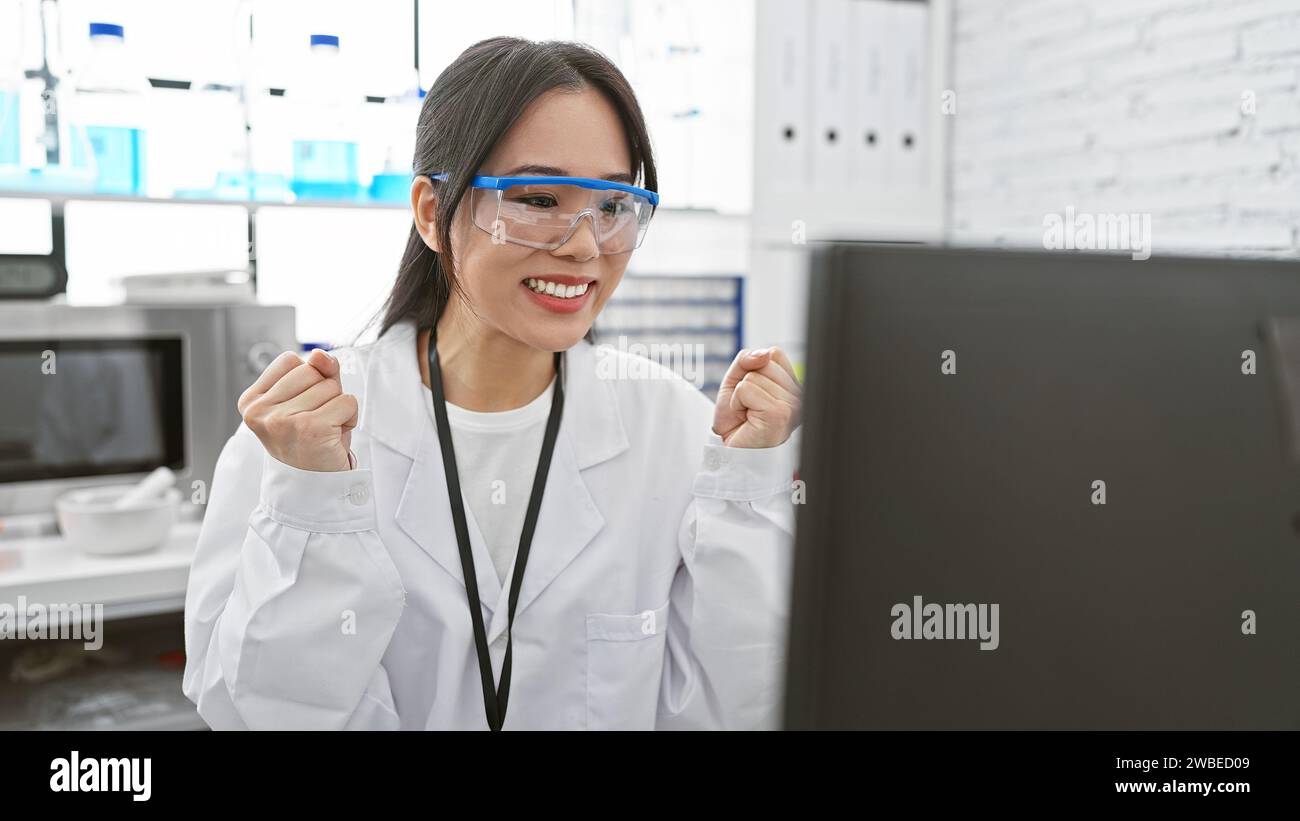 Excited asian woman scientist wearing lab coat and safety glasses in ...