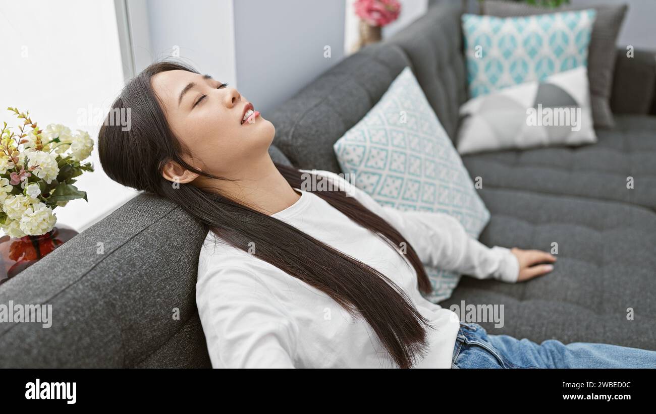 A relaxed asian woman lounging on a sofa in a modern living room ...
