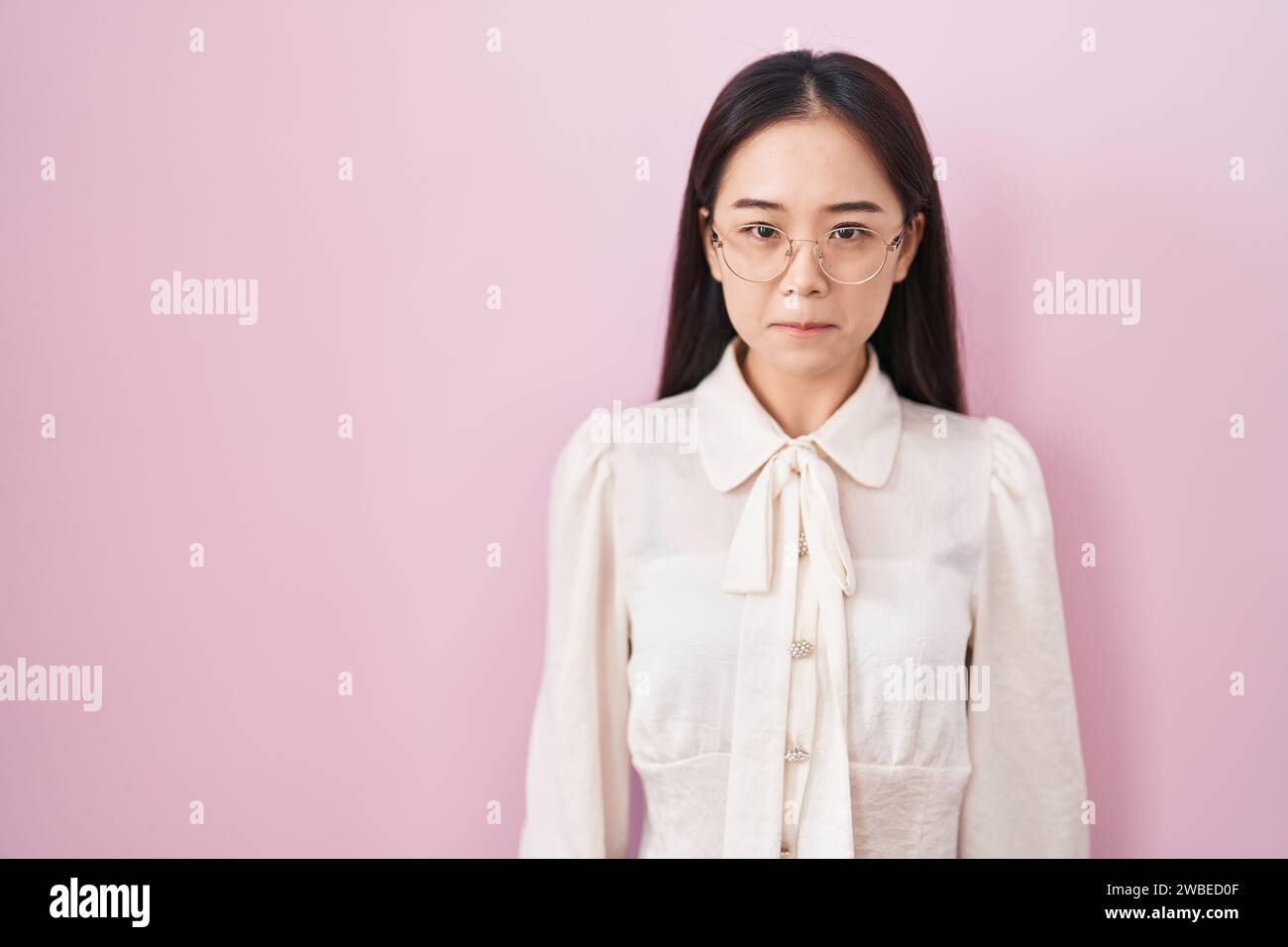 Young chinese woman standing over pink background skeptic and nervous ...
