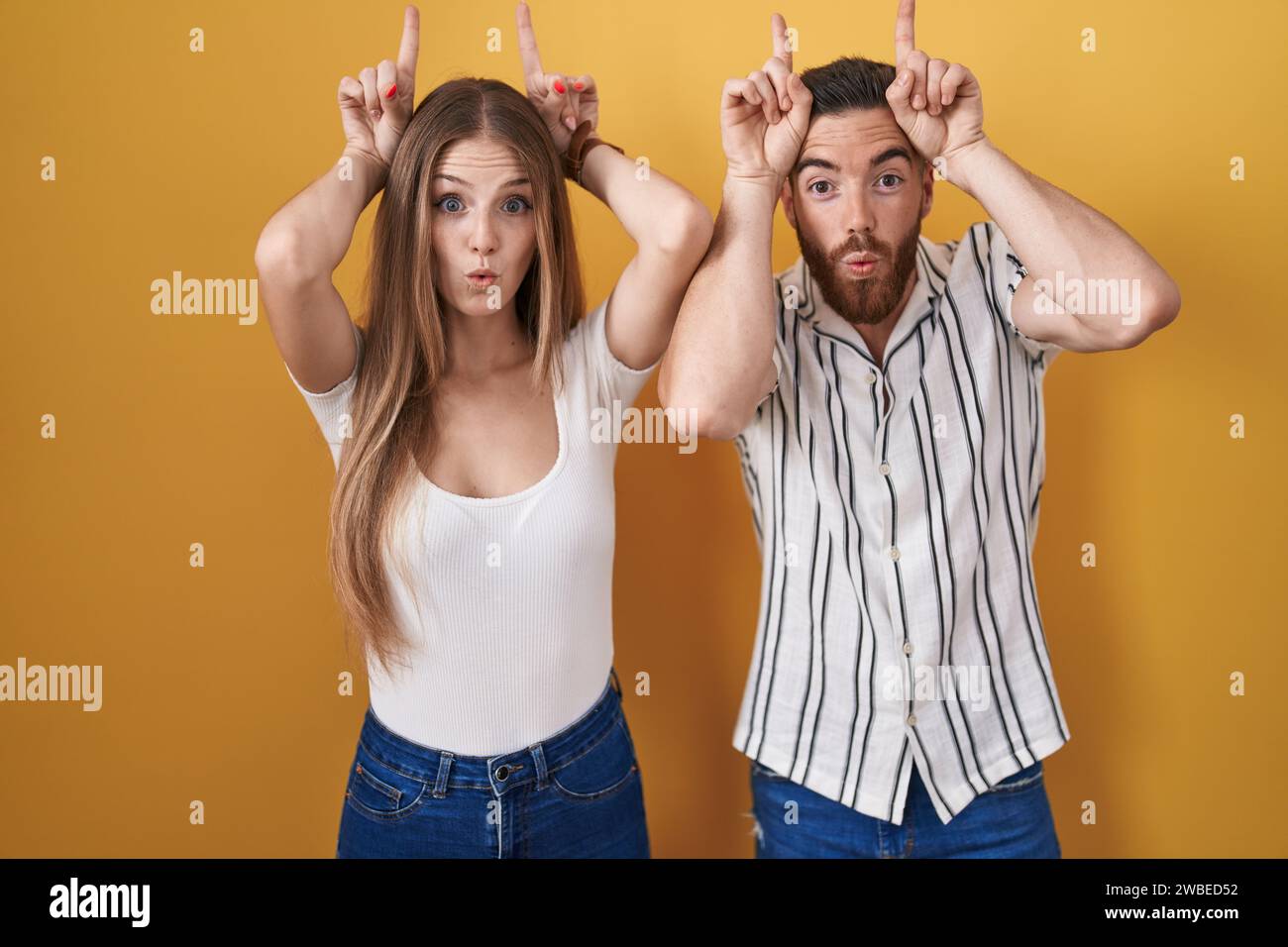 Young couple standing over yellow background doing funny gesture with ...