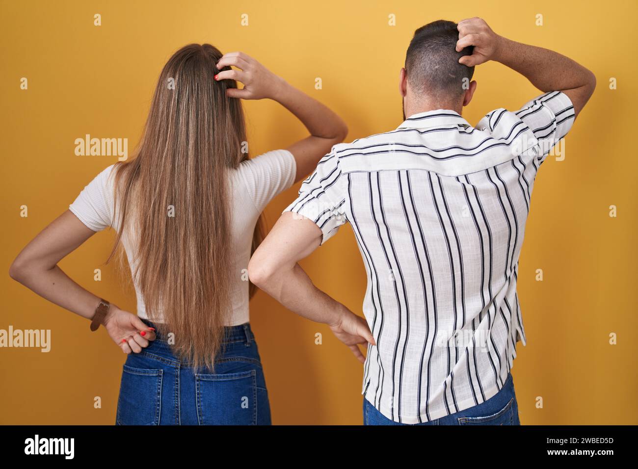 Young couple standing over yellow background backwards thinking about ...