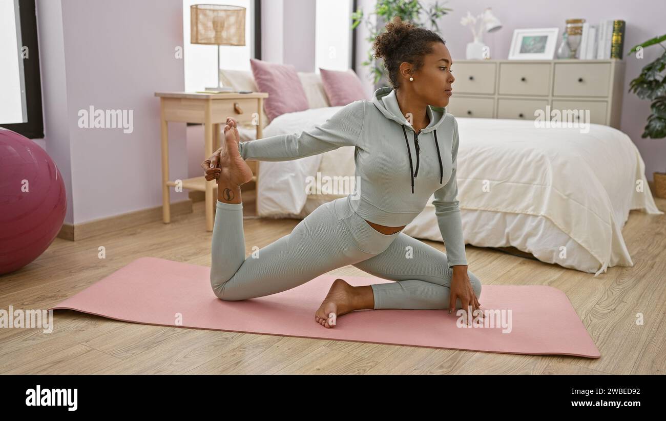 A fit woman in activewear stretches on a yoga mat in a well-lit bedroom ...