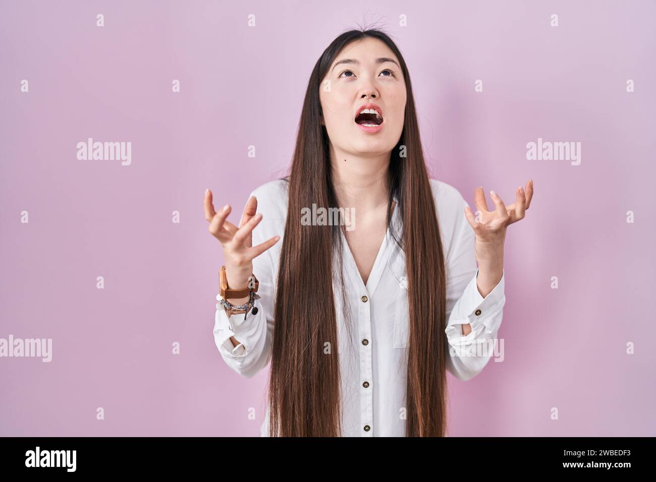 Chinese young woman standing over pink background crazy and mad ...