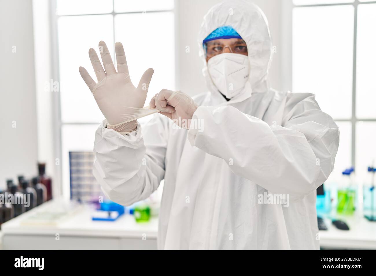 Young latin man scientist wearing covid protection uniform and gloves ...