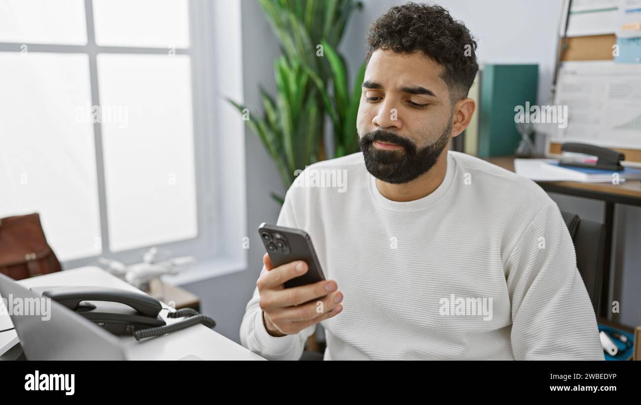 Focused hispanic man using smartphone in a modern office setting ...