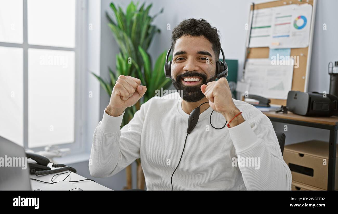 Handsome young man with beard in headset cheering in modern office ...