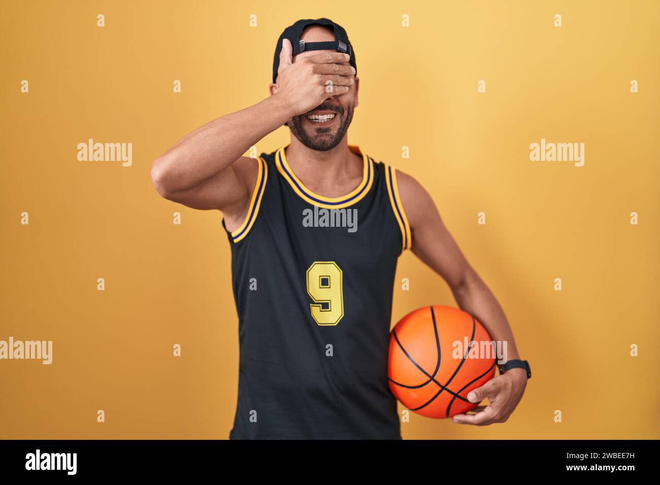 Middle age bald man holding basketball ball over yellow background ...