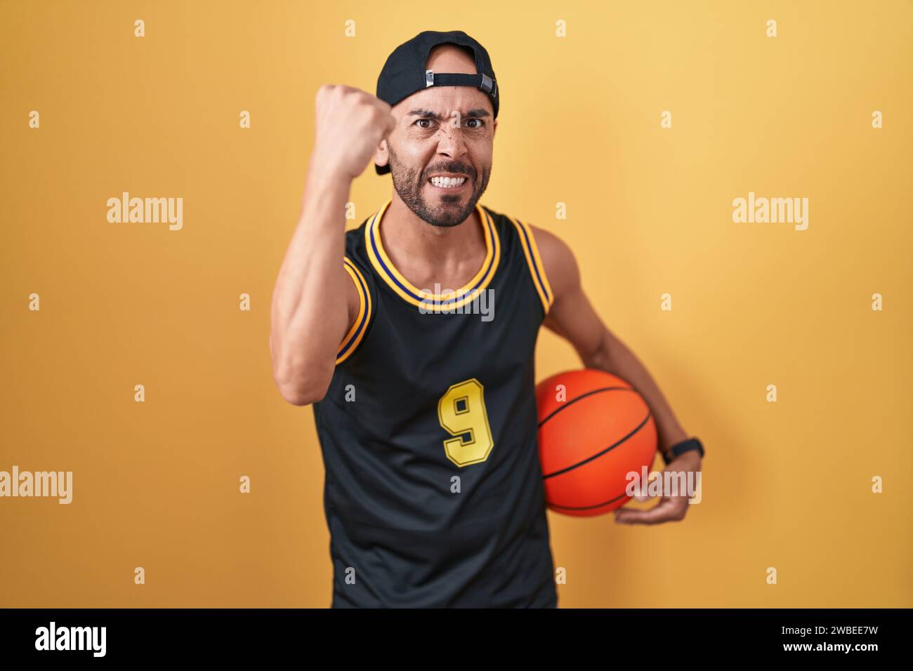 Middle age bald man holding basketball ball over yellow background ...