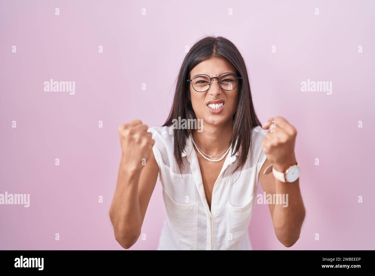 Brunette young woman standing over pink background wearing glasses ...