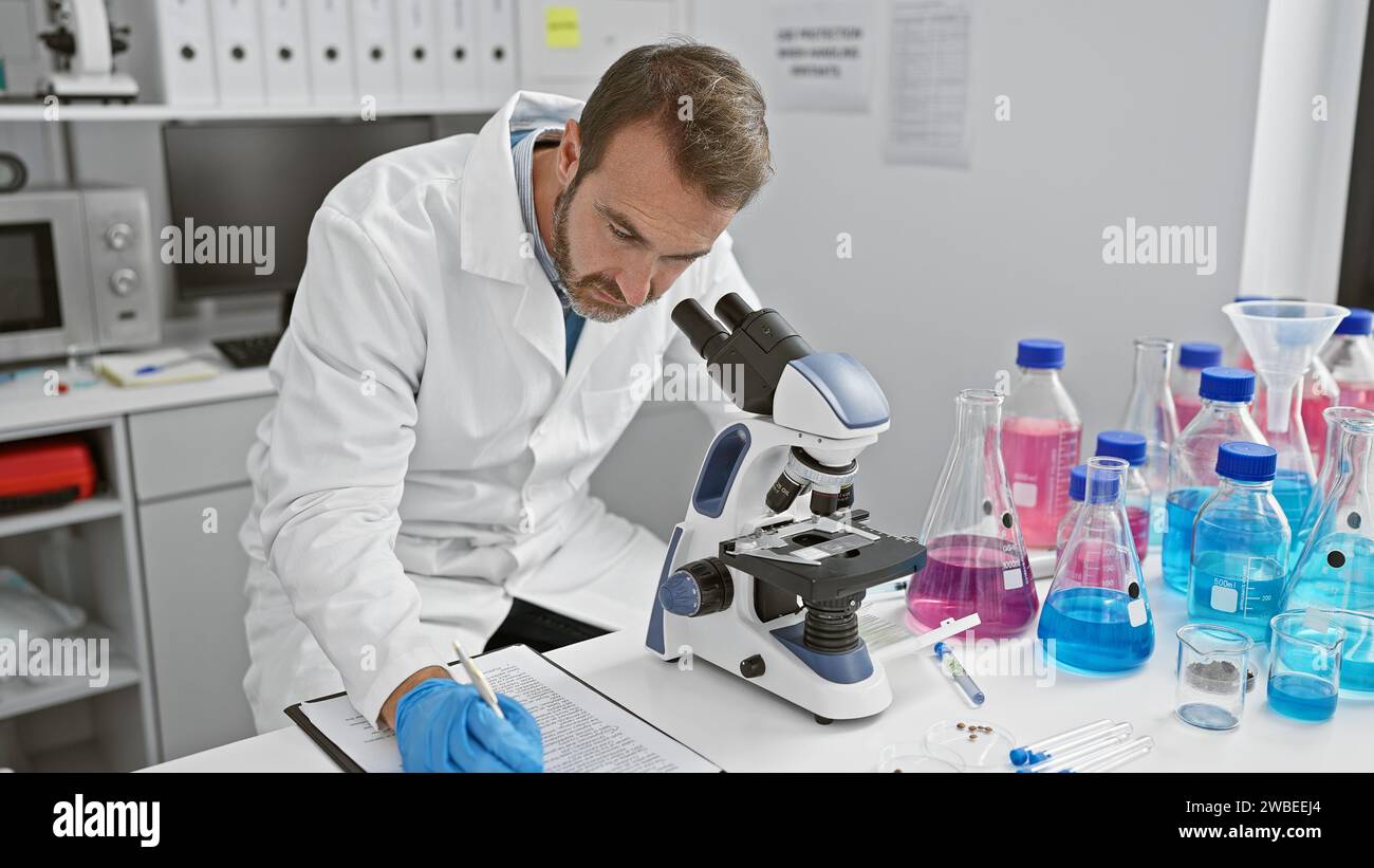 Focused hispanic man with beard using a microscope in a clinical ...