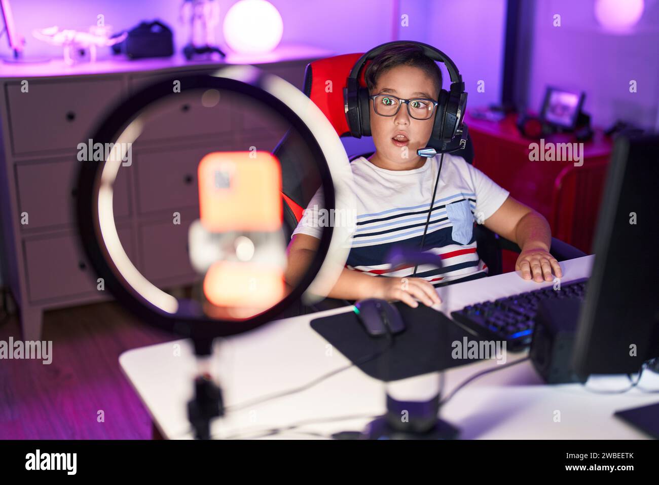 Young hispanic kid playing video games scared and amazed with open ...