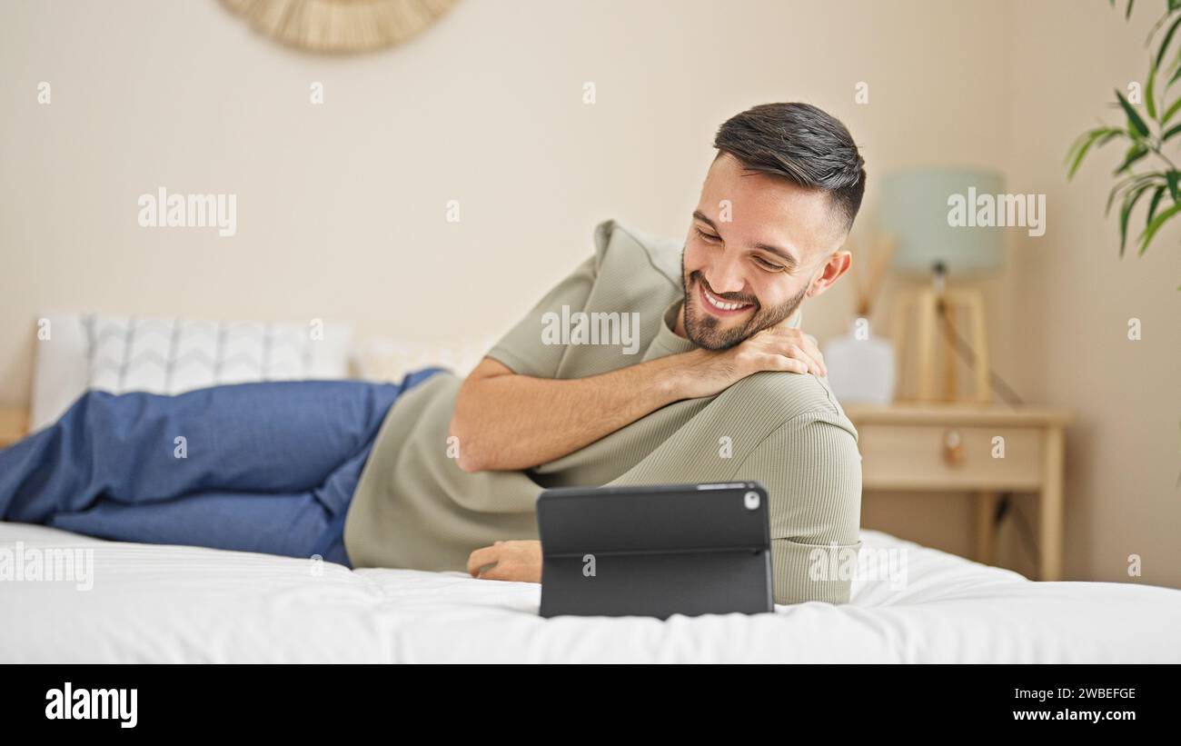 Young hispanic man watching video on touchpad lying on bed at bedroom Stock Photo - Alamy