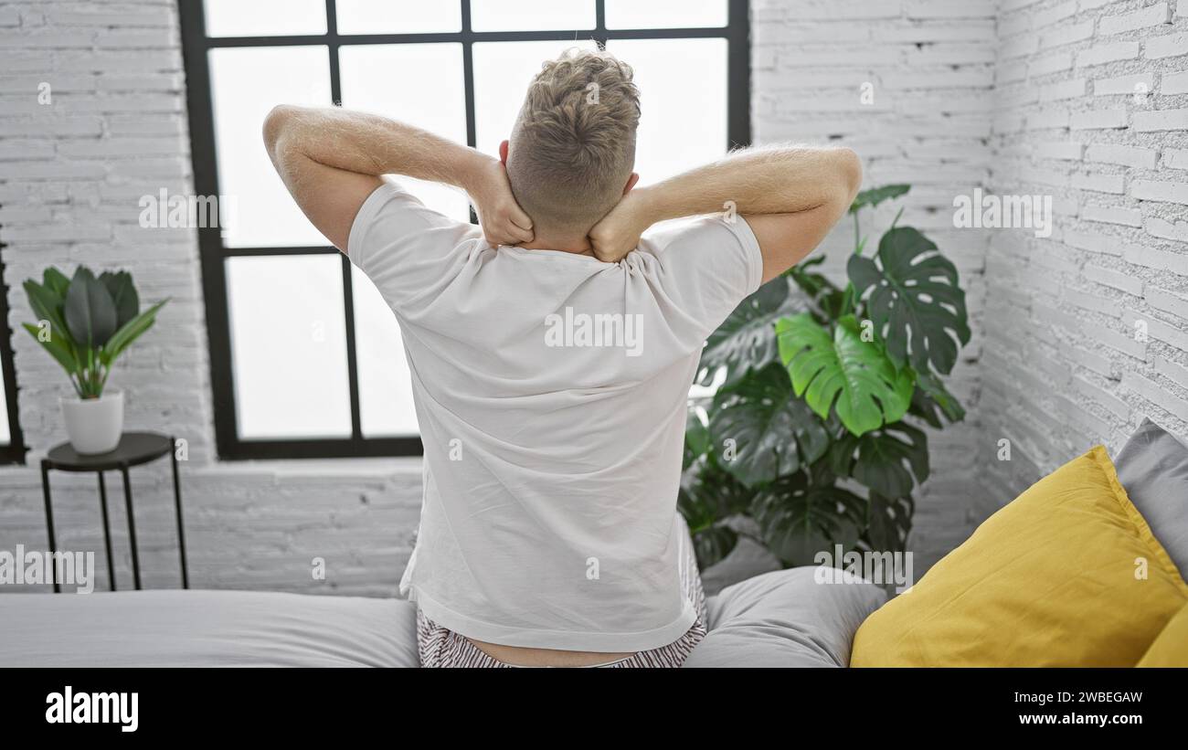 A young man stretches after waking up in a modern bedroom with white ...