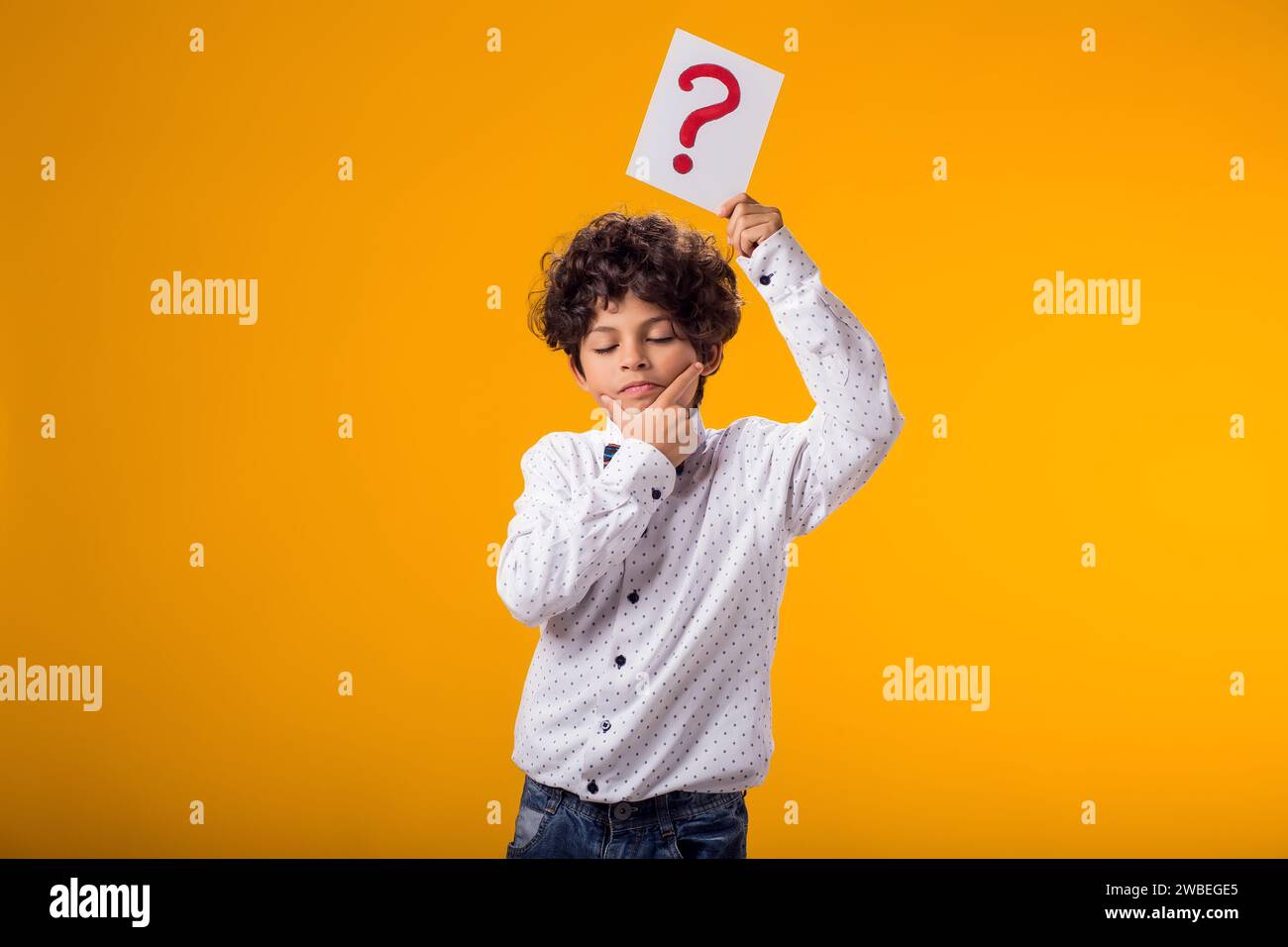 Portrait of child boy holding question mark card over yellow background ...