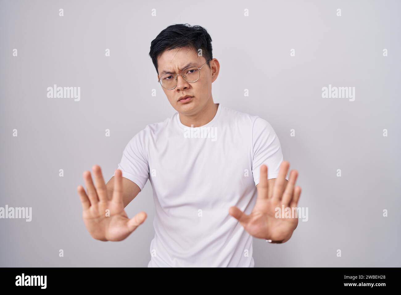 Young asian man standing over white background moving away hands palms ...
