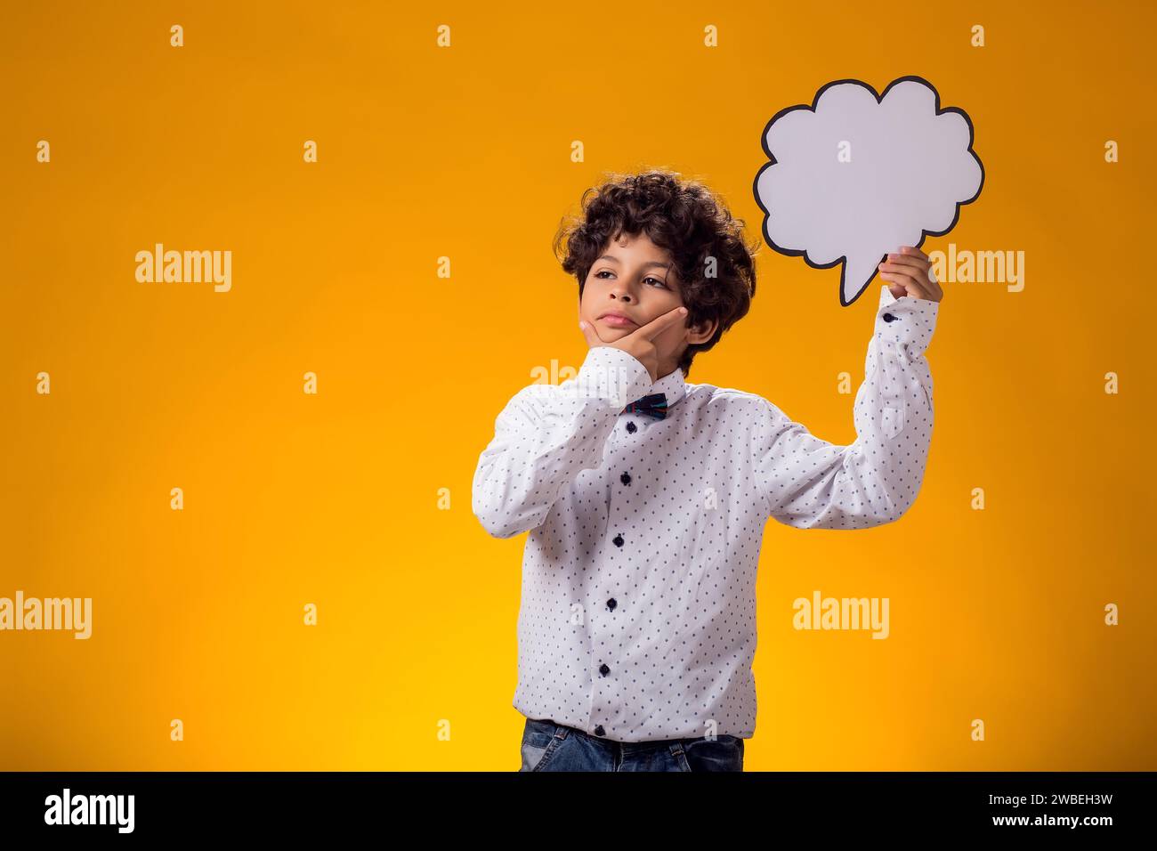 Thoughtful child boy holding speech bubble over yellow background ...