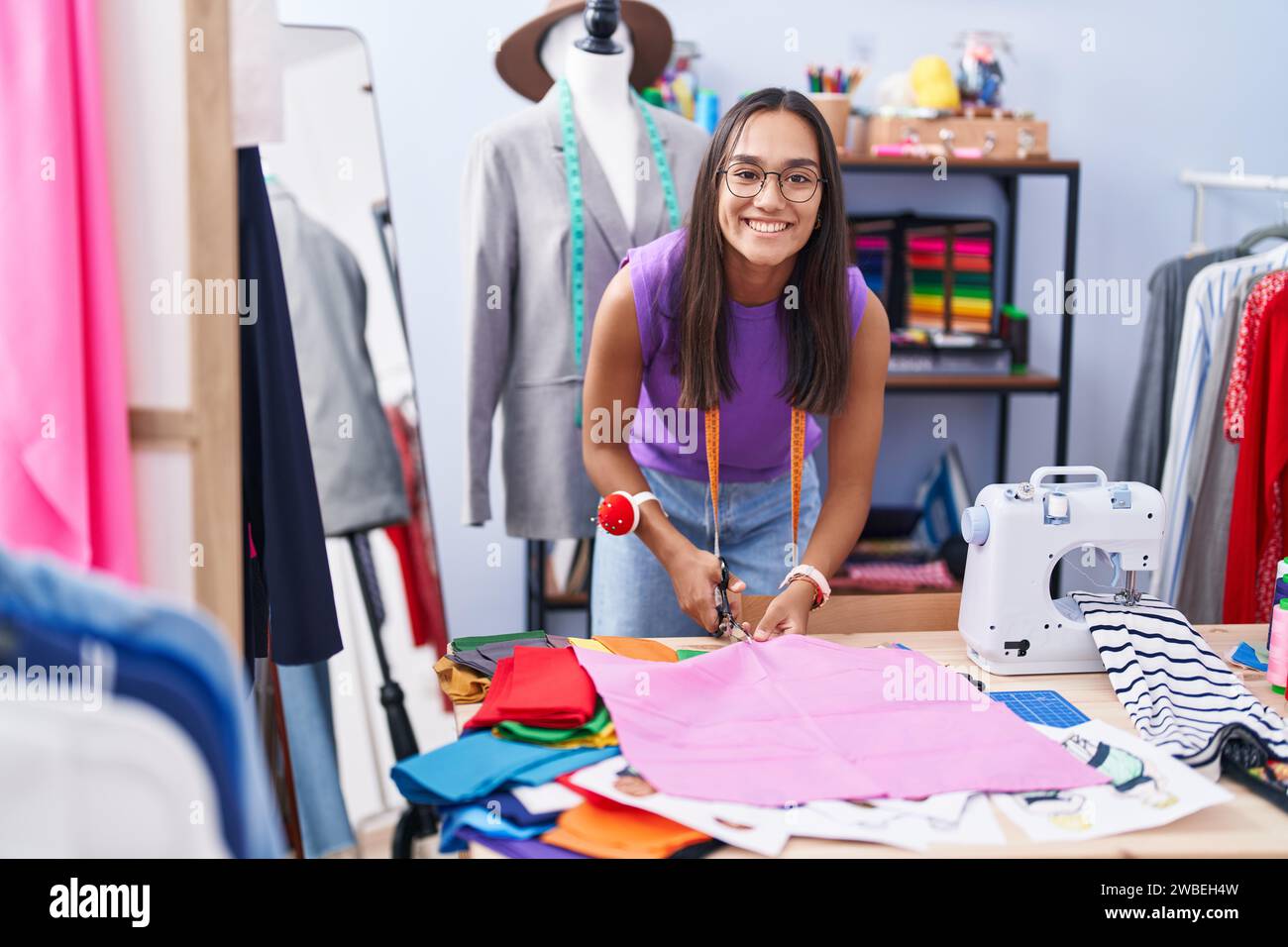 Young beautiful hispanic woman tailor smiling confident cutting cloth ...