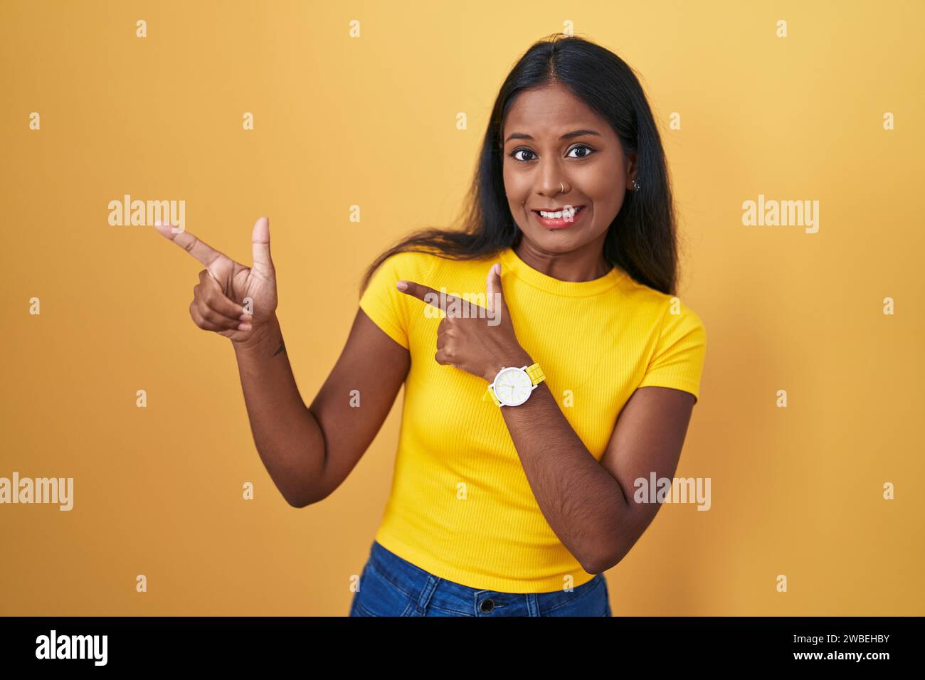 Young indian woman standing over yellow background pointing aside ...