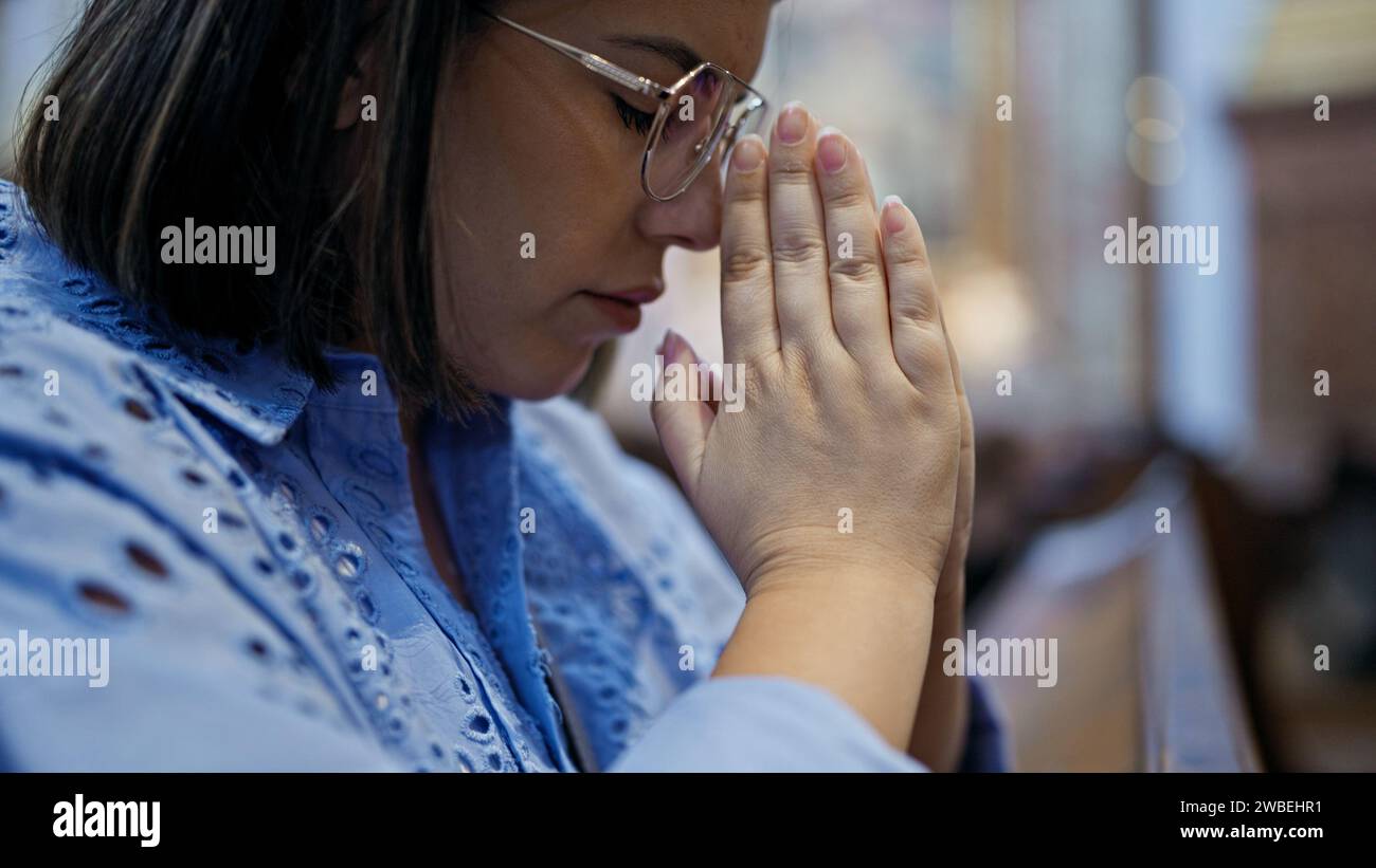 Young beautiful hispanic woman praying on a church bench at St. Karl ...