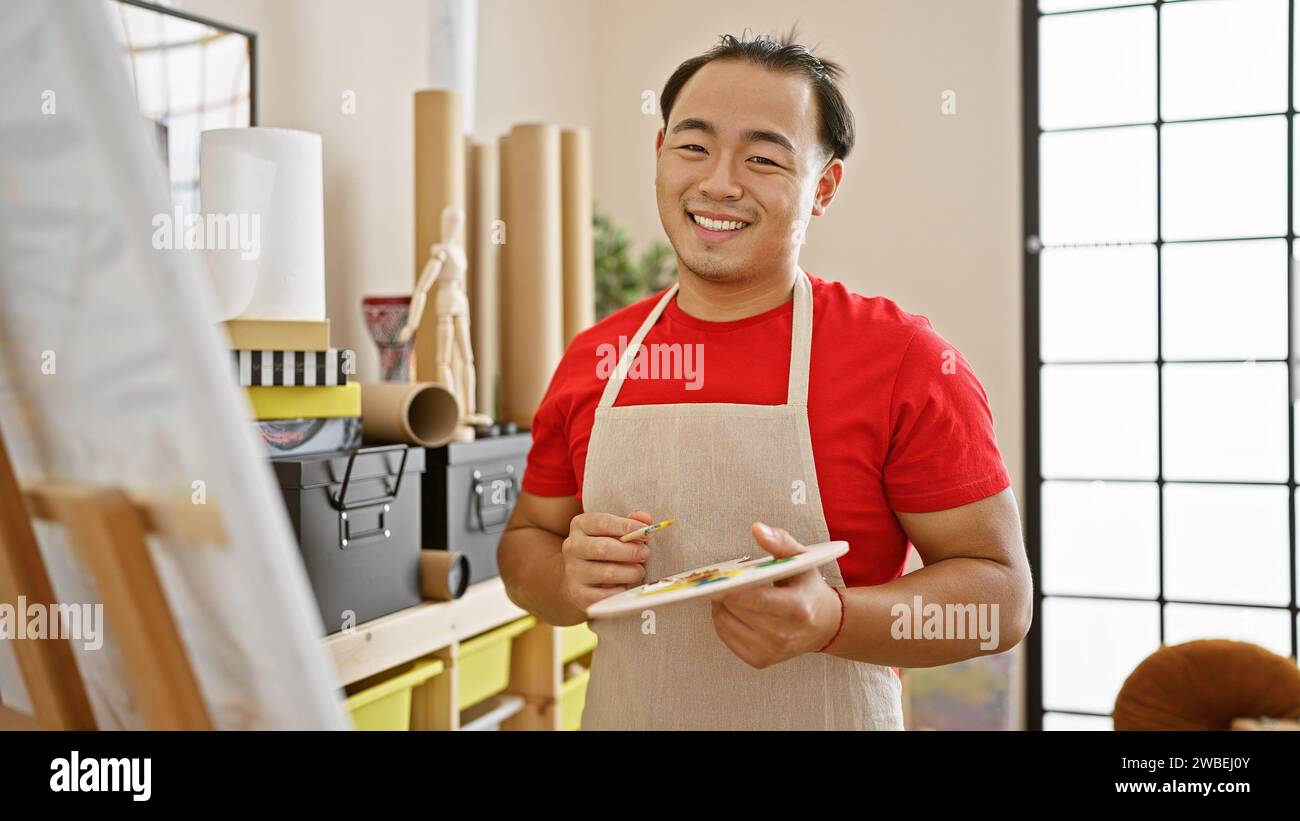Smiling, confident young chinese man passionately draws in art studio ...