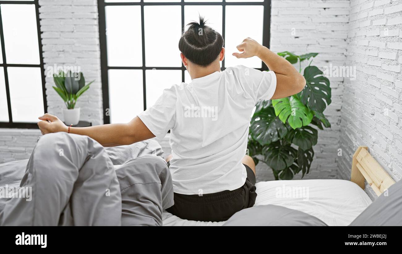 Cozy morning as a handsome young chinese man wakes up, stretches arms ...
