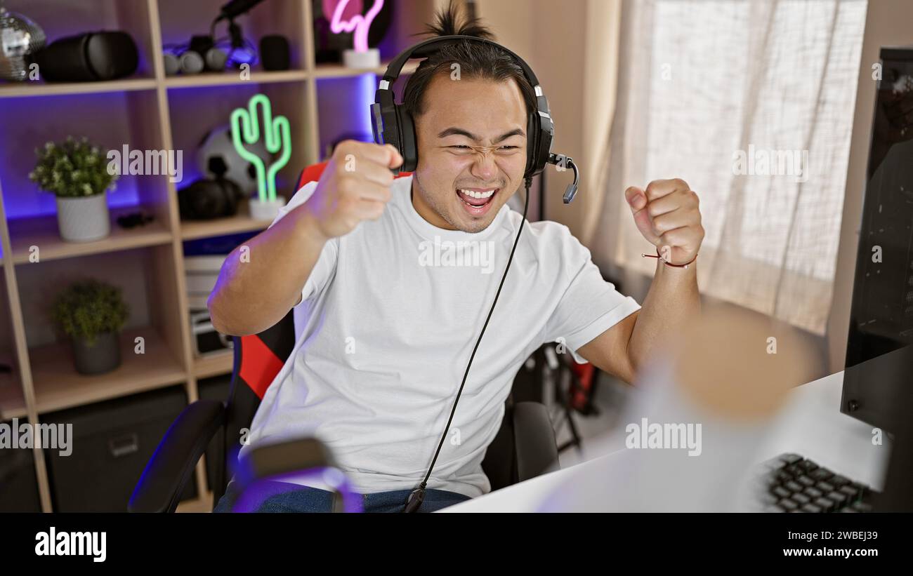 Triumphant young chinese streamer, headset worn, celebrating victorious ...