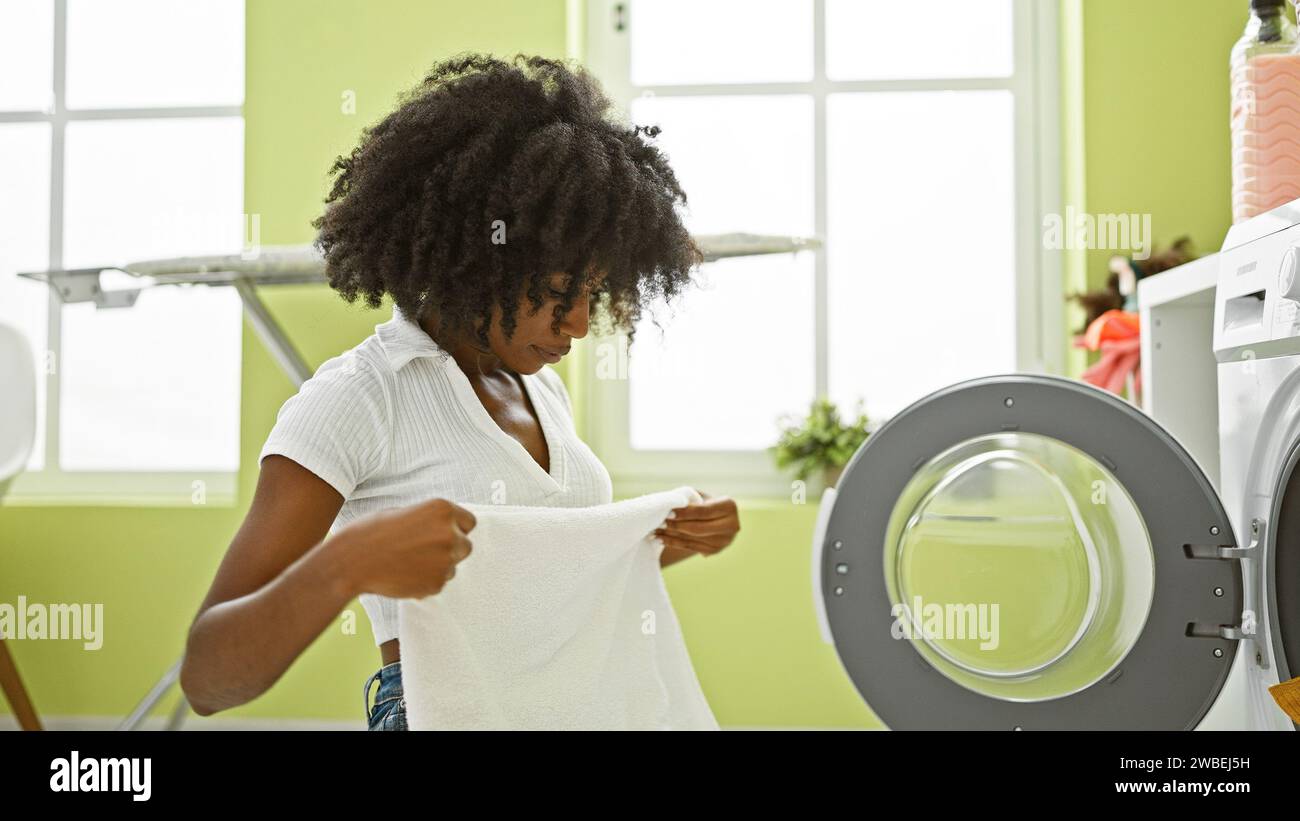 African american woman washing clothes folding towel at laundry room ...