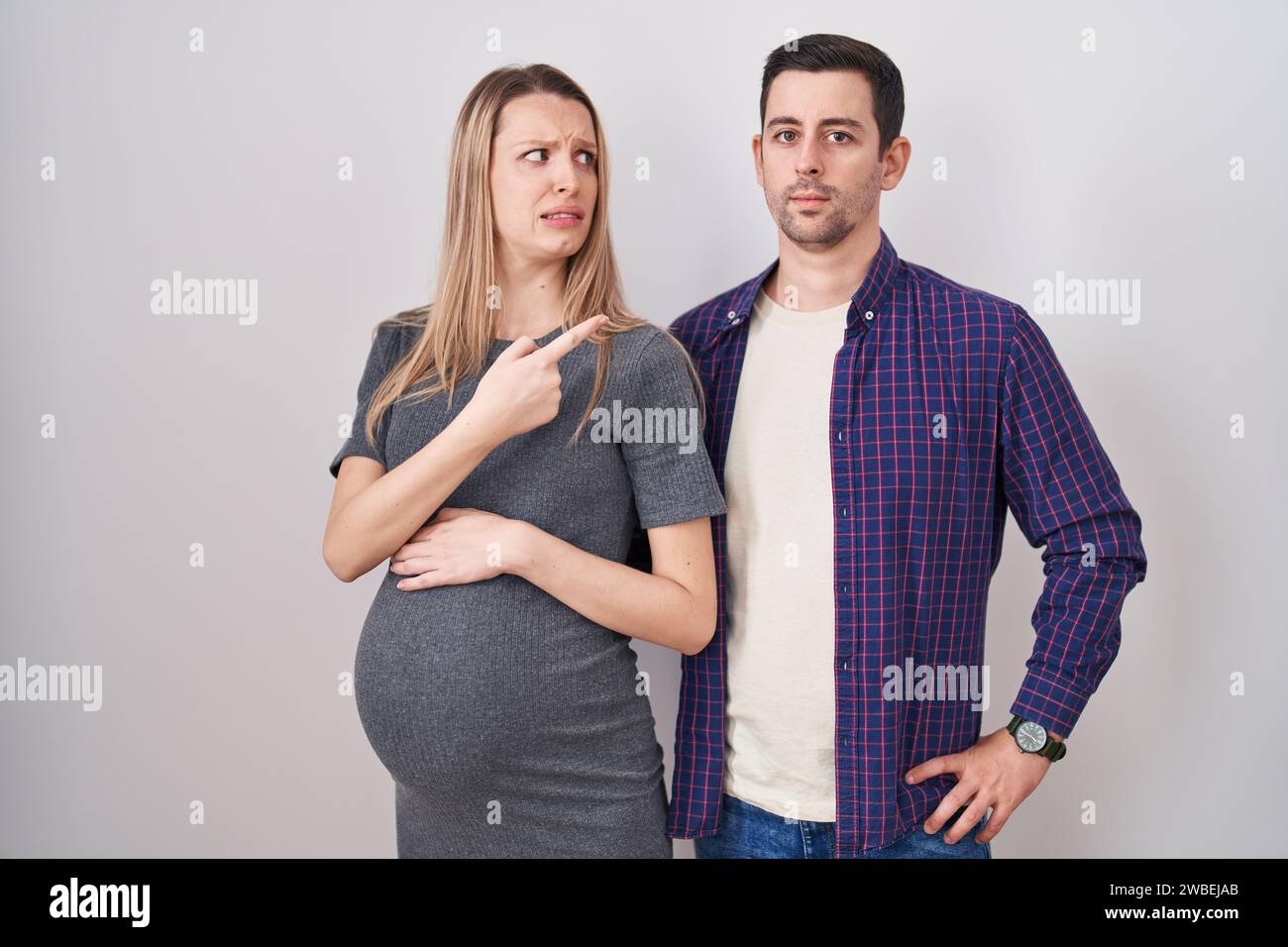 Young couple expecting a baby standing over white background pointing ...