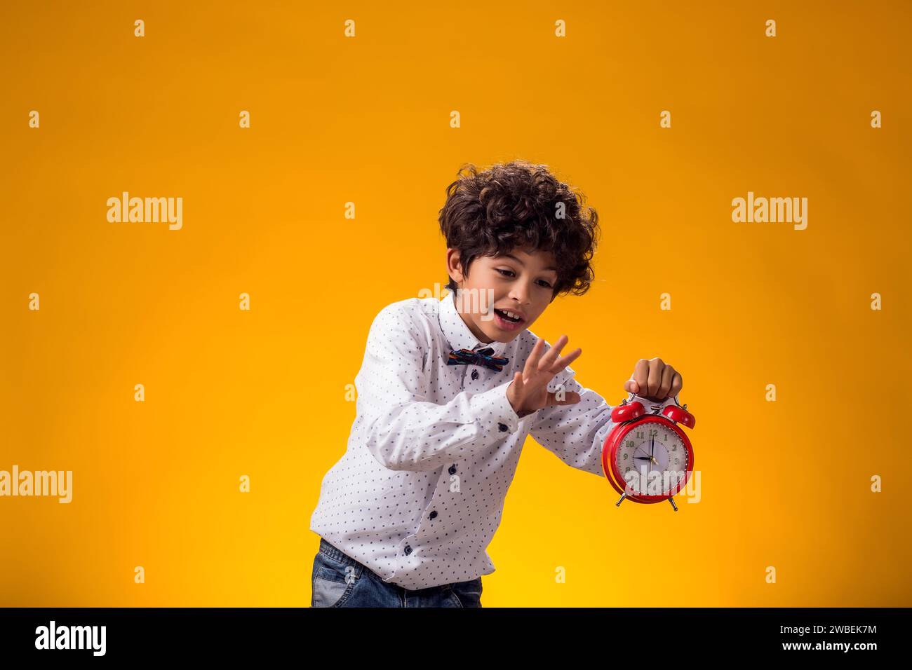 Portrait of child boy holding alarm clock over yellow background. Time ...